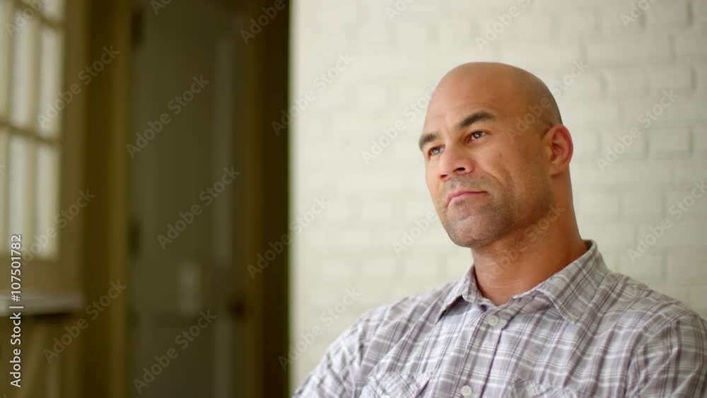 Handsome mixed-race bald man sitting, smiling and looking around in ...