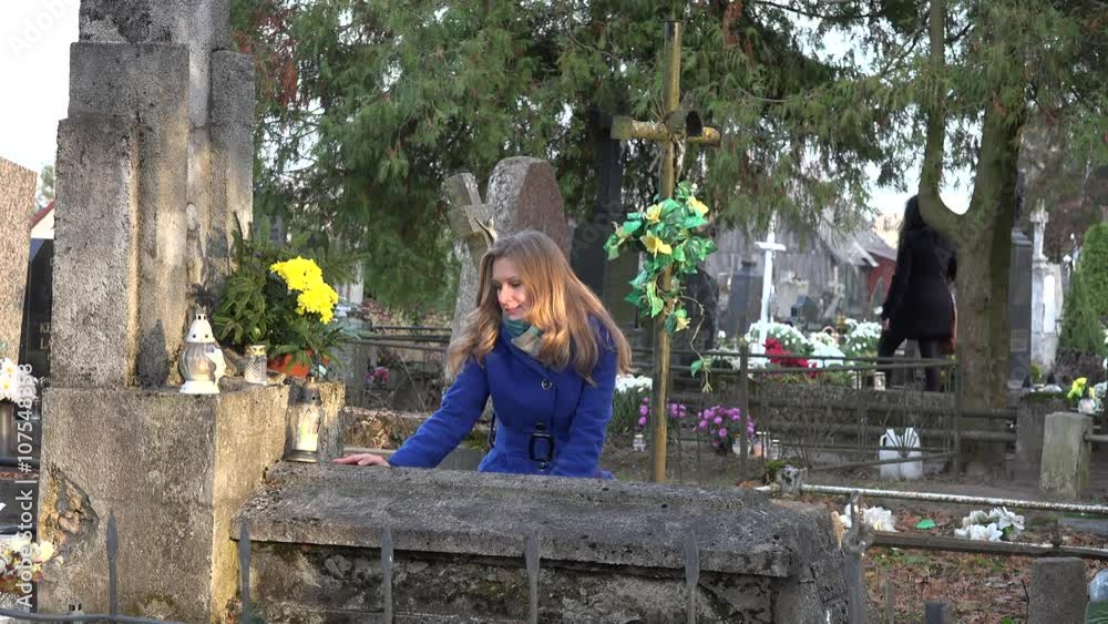 Young sad woman on knees caress old grave with palm in cemetery. Static ...