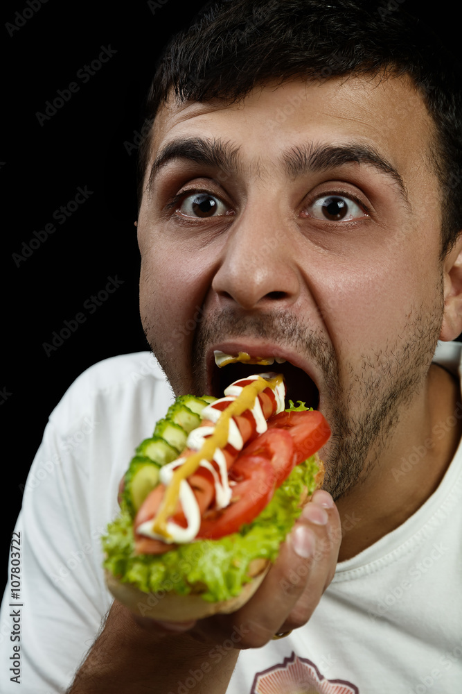 Young armenian man eating a messy hotdog isolated on black background ...