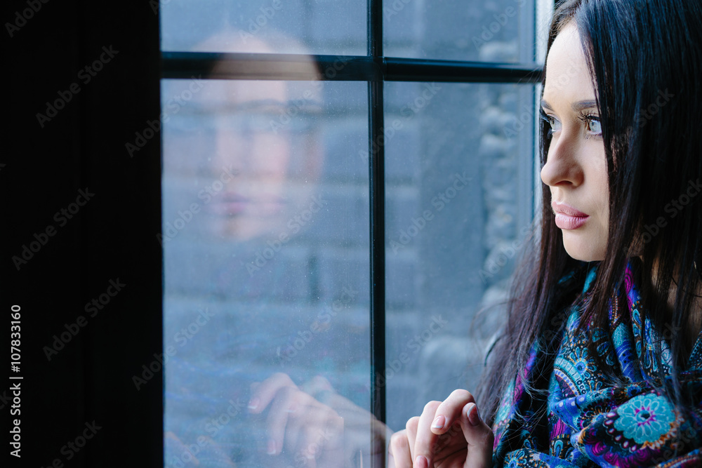 Sad beautiful woman looking through a window and thinking about ...