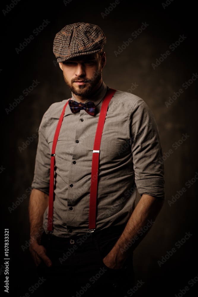 Serious old-fashioned man in tweed hat wearing suspenders and bow tie ...