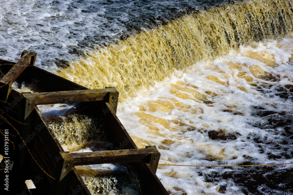 Wooden fish ladder with flowing water beside a reservoir overflow. This ...