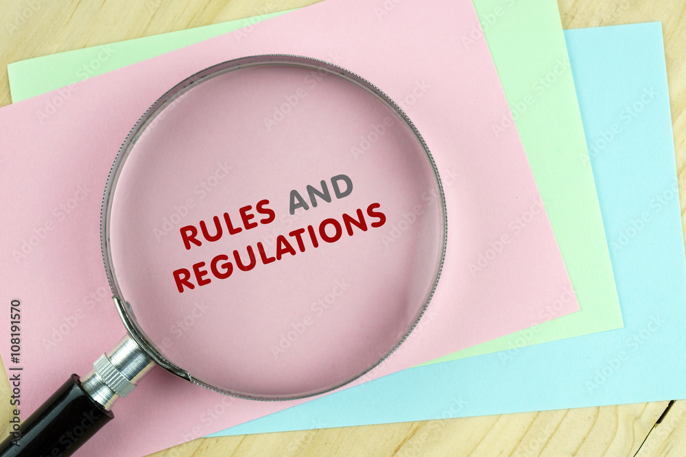Word RULES and REGULATIONS on colored paper with magnifying glass ...