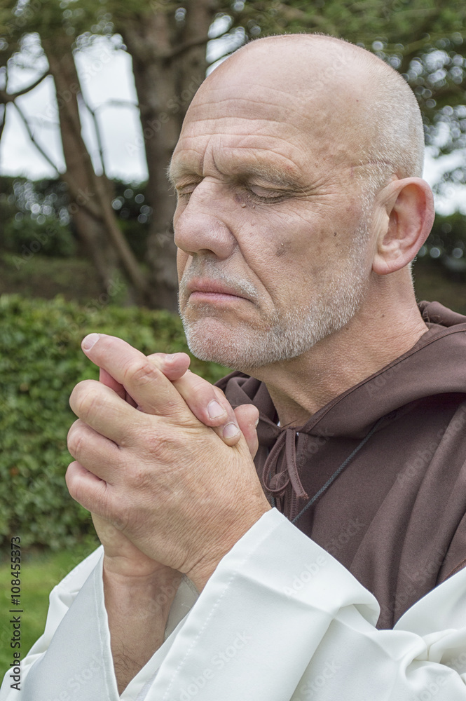 Portrait image of a mature man dressed as a monk, praying in an outdoor ...