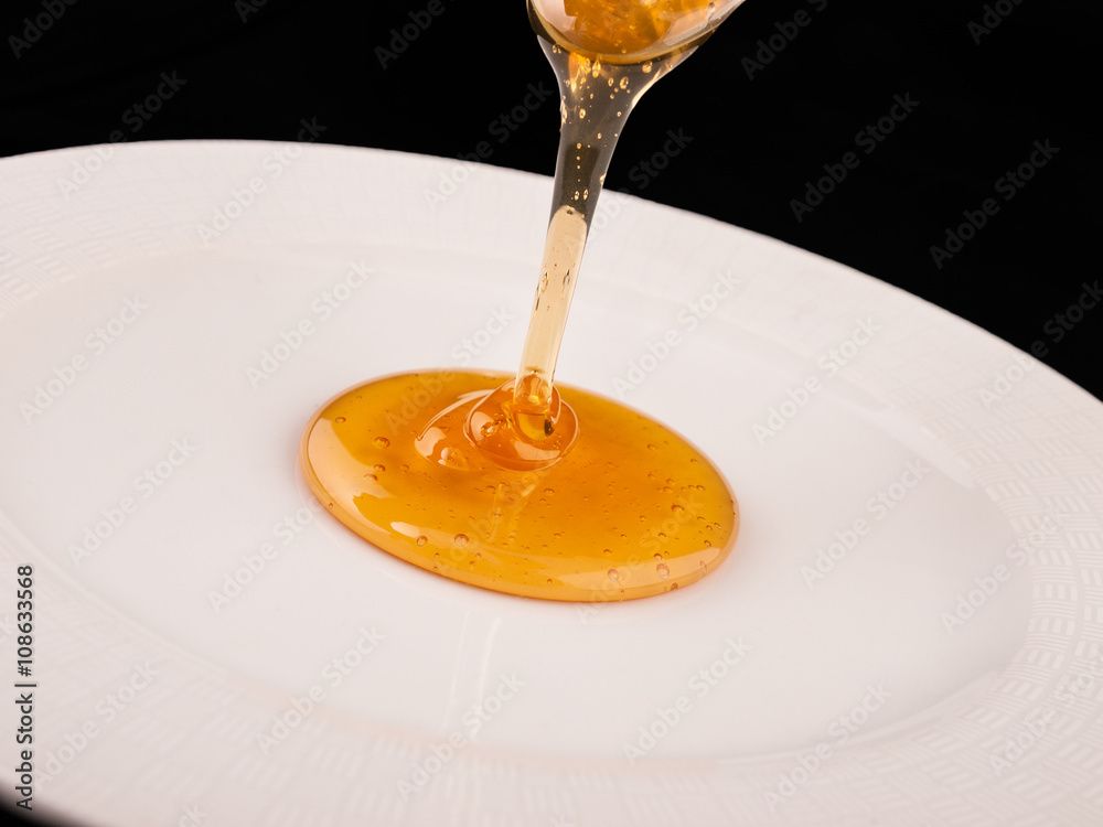 Miel líquida derramándose sobre plato blanco, fondo negro. Vista ...