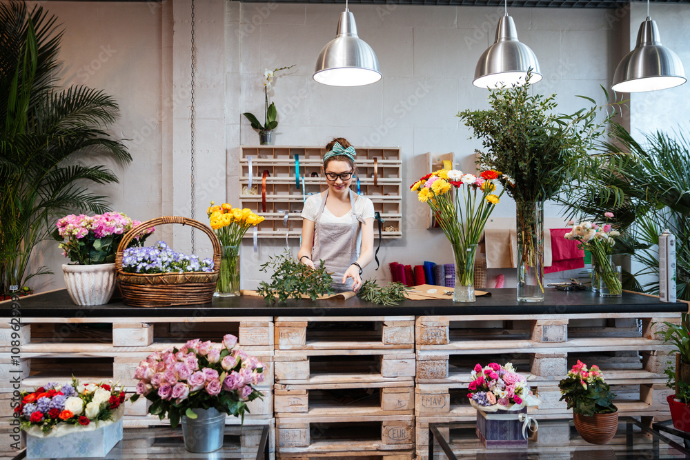 Smiling woman florist standing and working in flower shop Stock Photo ...