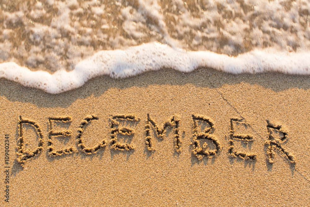 December - word drawn on the sand beach with the soft wave. Months ...
