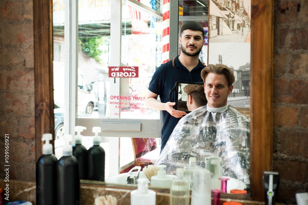 Mirror image of barber using mirror to show smiling customer haircut ...