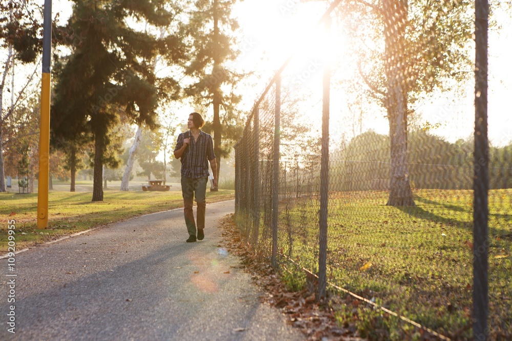 Full length front view of young man walking on pathway through park ...