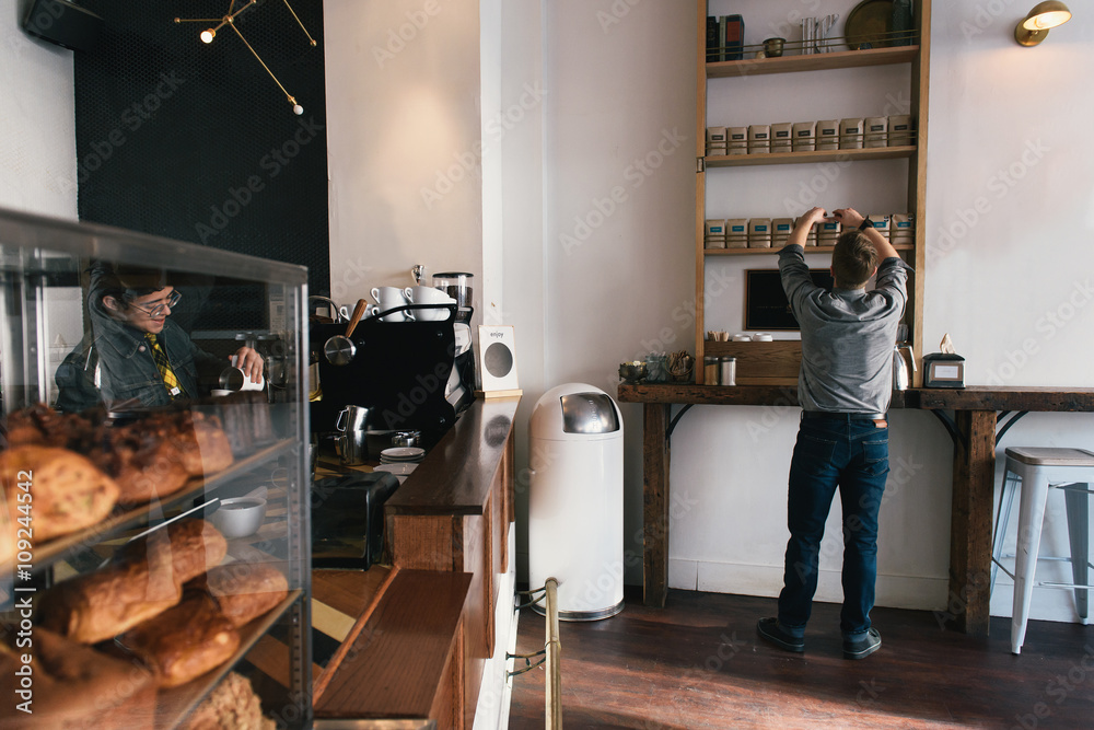 Rear view of waiter removing coffee bean packet from coffee shop shelf ...
