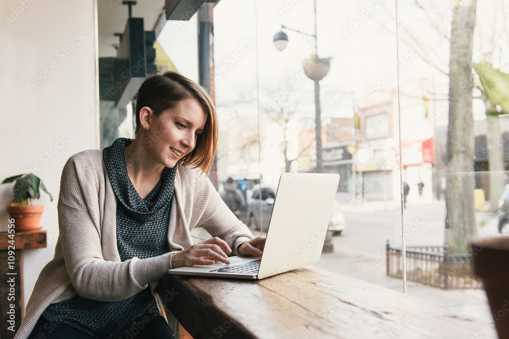 Female customer sitting in coffee shop window seat typing on laptop ...