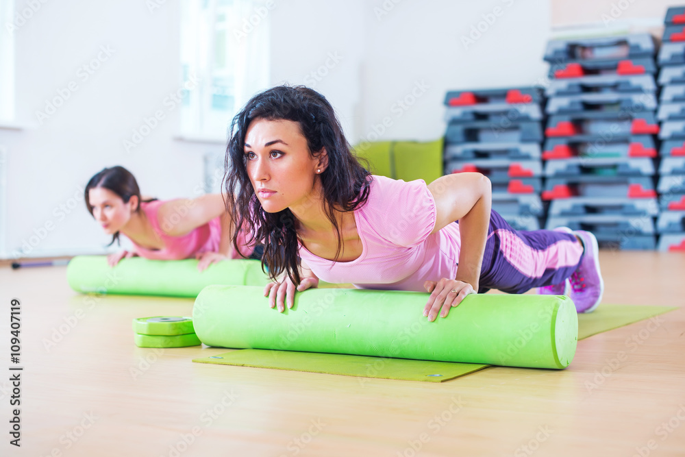 Fit woman exercising on floor using foam roller doing push ups triceps ...