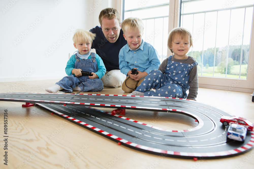 Mid adult man and three young children playing with toy racing cars on ...