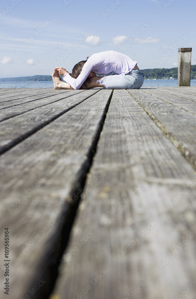 Surface level side view of mature woman sitting on pier bending over ...