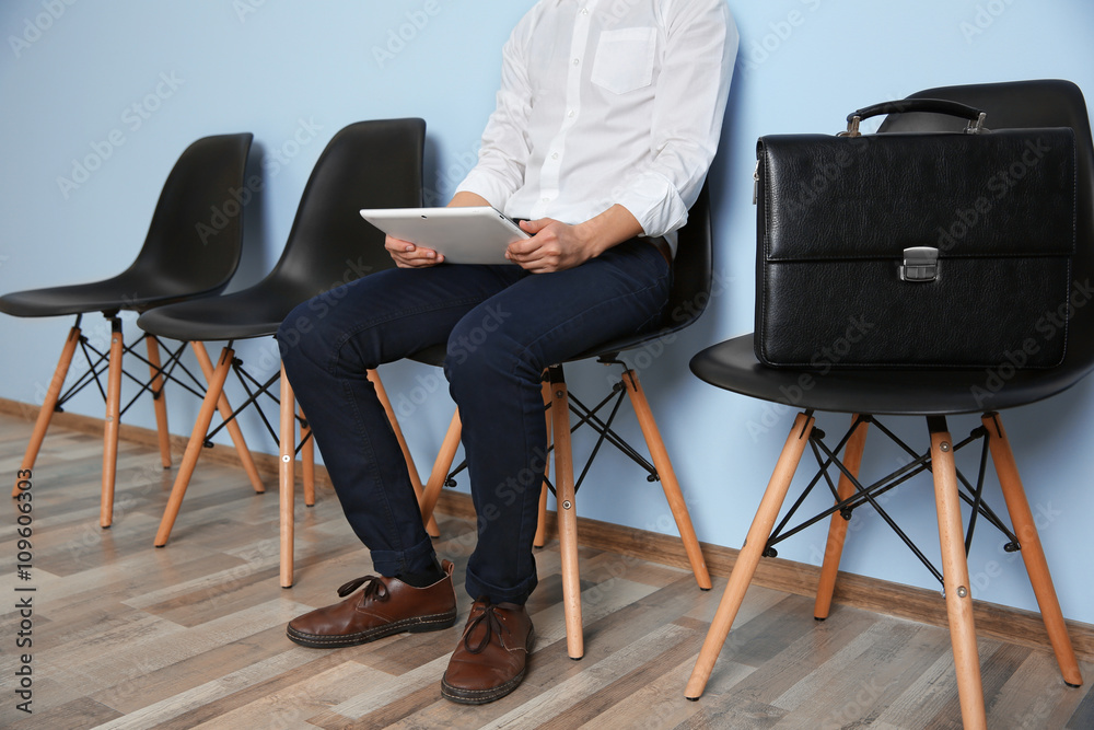 Young man in suit sitting on chair with tablet and waiting for job ...