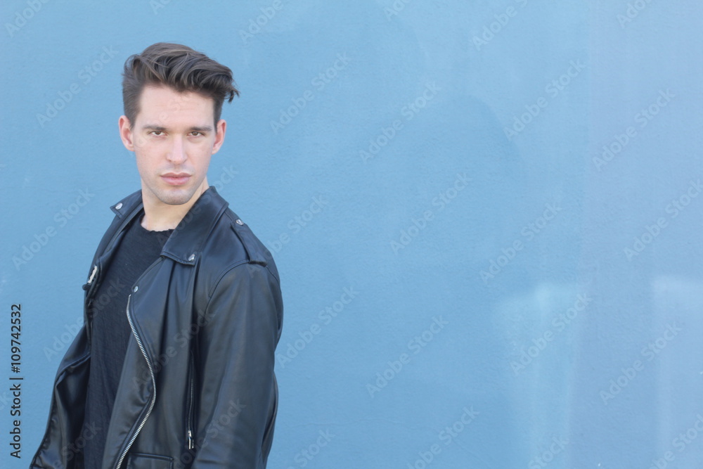 Trendy relaxed young man with a modern haircut standing against a blue ...