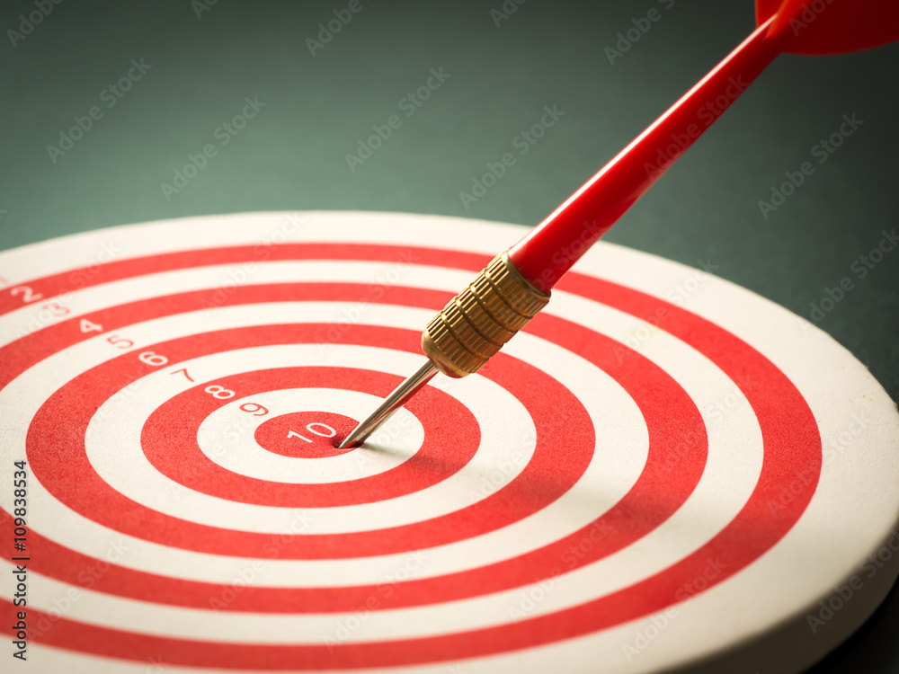Selective focus of red dart arrow hitting target center of dartboard on ...