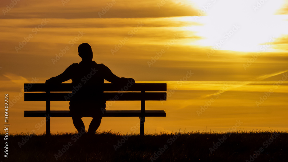Silhouette man sitting on a bench looking up at the sunset Stock Photo ...