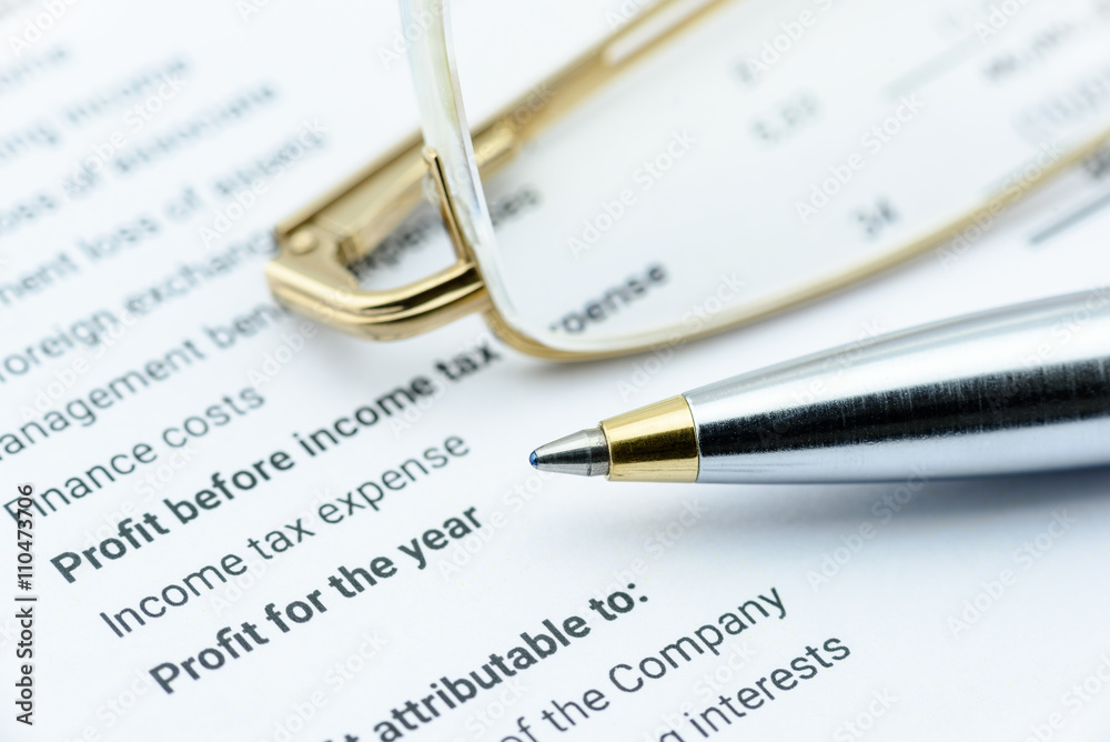 Blue ballpoint pen and eye grasses on a company's financial report, in ...