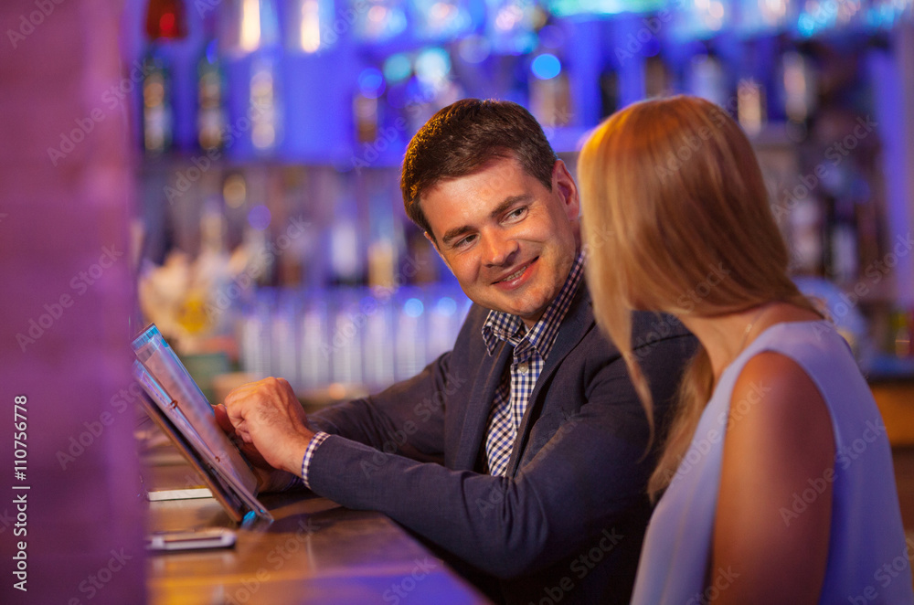Smiling man at bar counter with menu looking at blonde unrecognizable ...