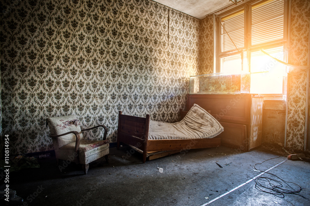 Abandoned room with broken bed, armchair and chest of drawers to a dry ...