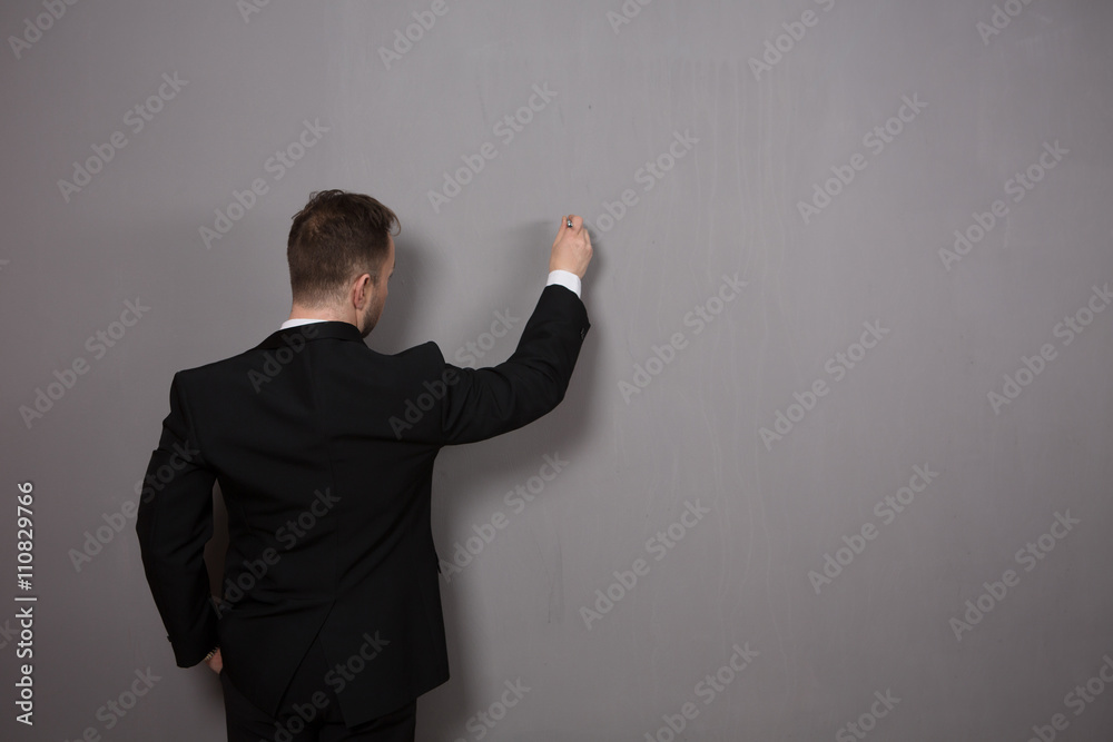 Back view of businessman writing something on wall in studio. Young man ...