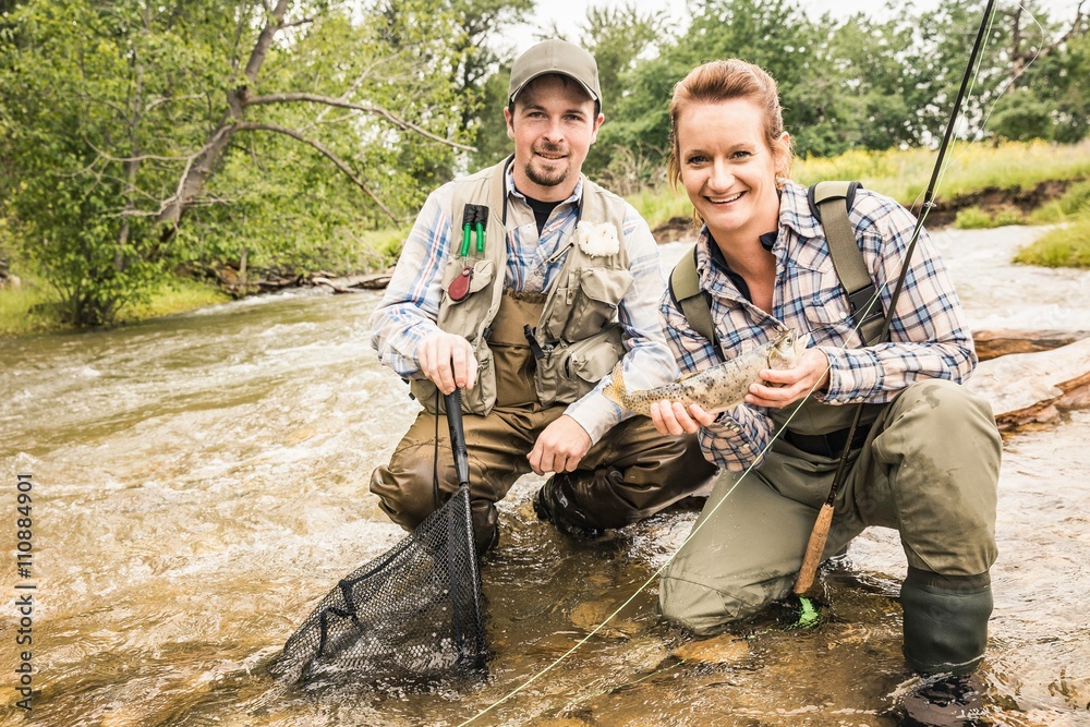 Couple crouching in river holding freshly caught fish looking at camera ...