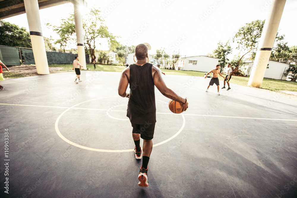 Full length rear view of young man walking on basketball court holding ...