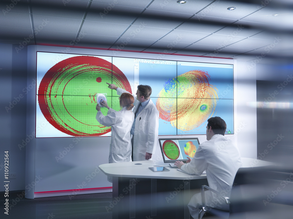 Scientists in meeting in front of graphical display of silicon wafer on ...