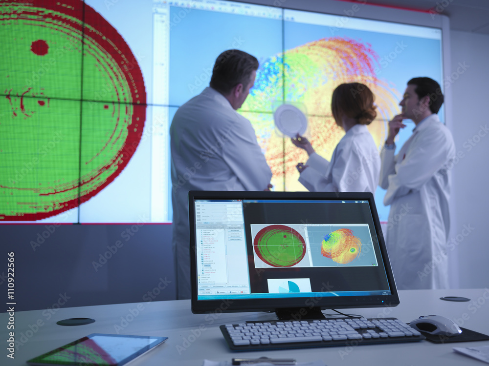Scientists in meeting in front of graphical display of silicon wafer on ...