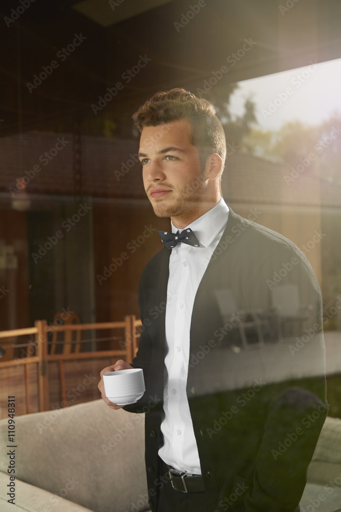 Shot through window of man standing looking out at the view holding cup ...