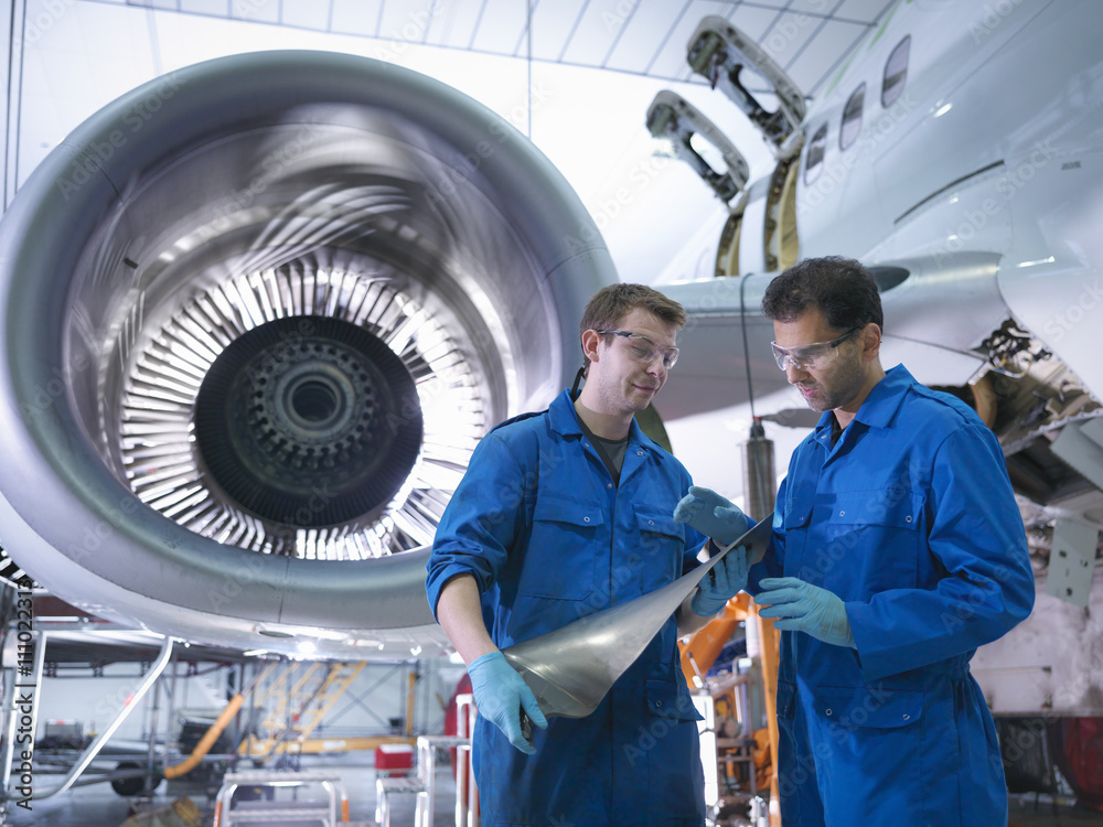 Engineers inspecting jet engine turbine blade in aircraft maintenance ...