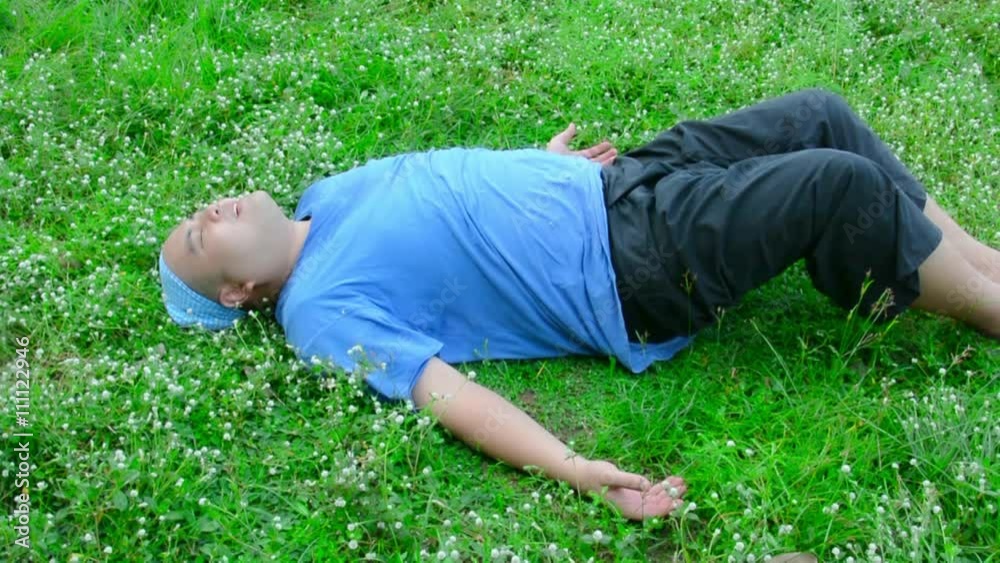 A fat bald head Thai man is lying on the soft green grass, relaxing and ...