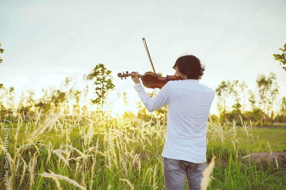 Young man playing the violin at sunrise standing with his backside to ...