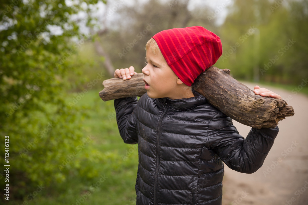 kid boy in red hat carrying big tree branch. Outdoor activites with ...