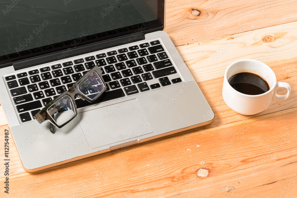 Work desk with laptop computer, eyeglasses and hot coffee cup. Top view ...