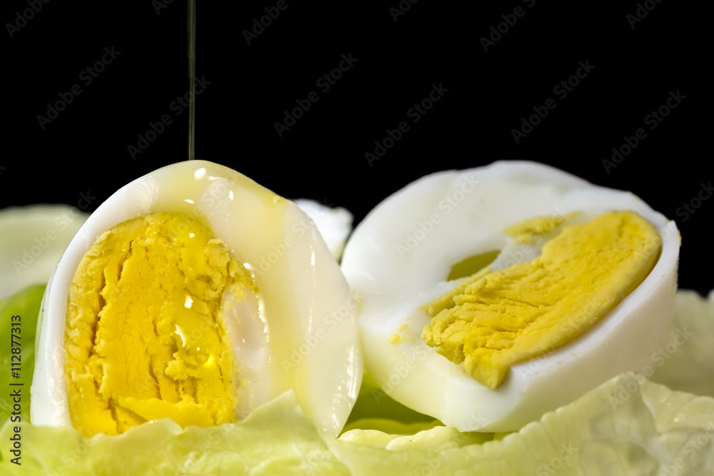Trickle of Extra Virgin olive oil falling over a hard boiled egg cut in ...