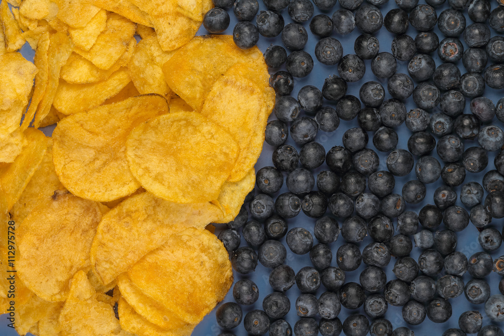 Texture fatty chips and fresh blueberries. Poor unhealthy diet and a ...
