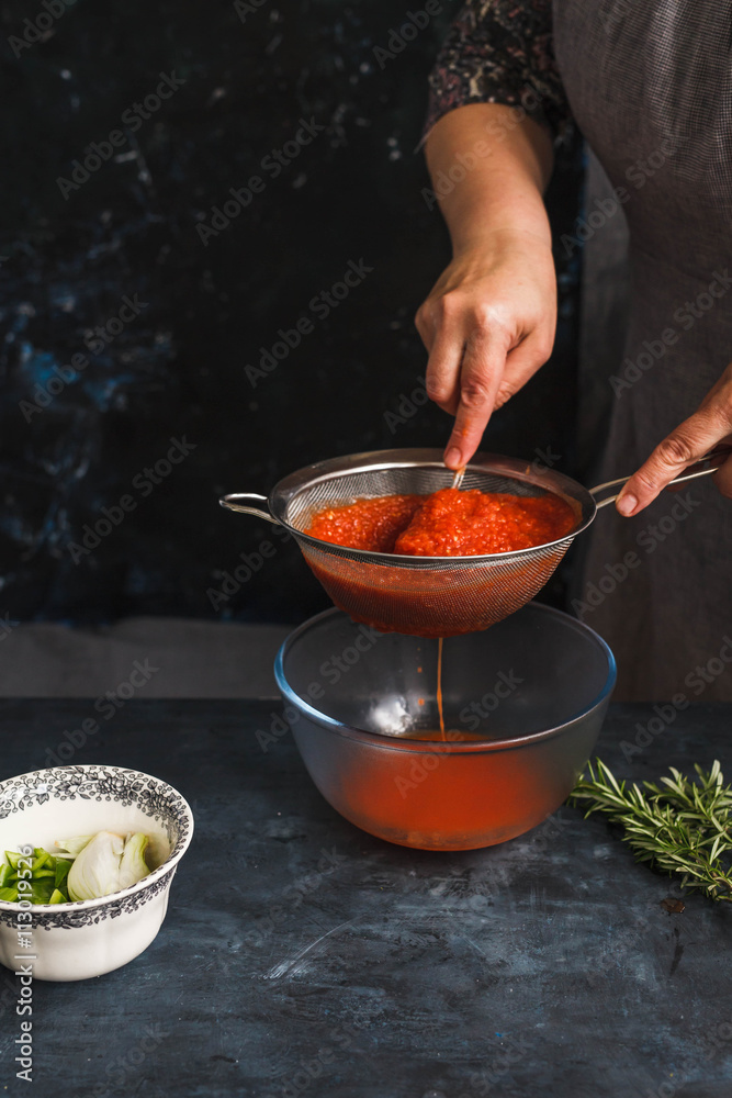 Straining blended tomatoes over a bowl glass. foto de Stock | Adobe Stock