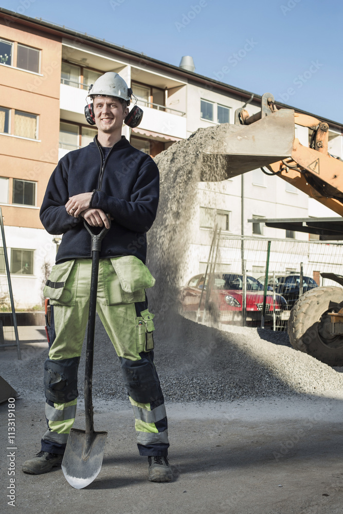 Full length portrait of smiling construction worker with shovel ...