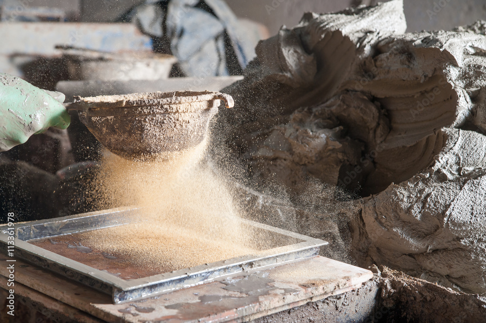 Red brick artisan strewing sawdust at the base of a mould before ...