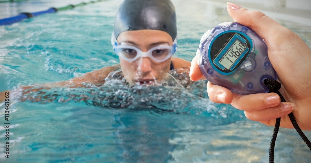 Composite image of a hand holding a timer against fit swimmer coming up ...