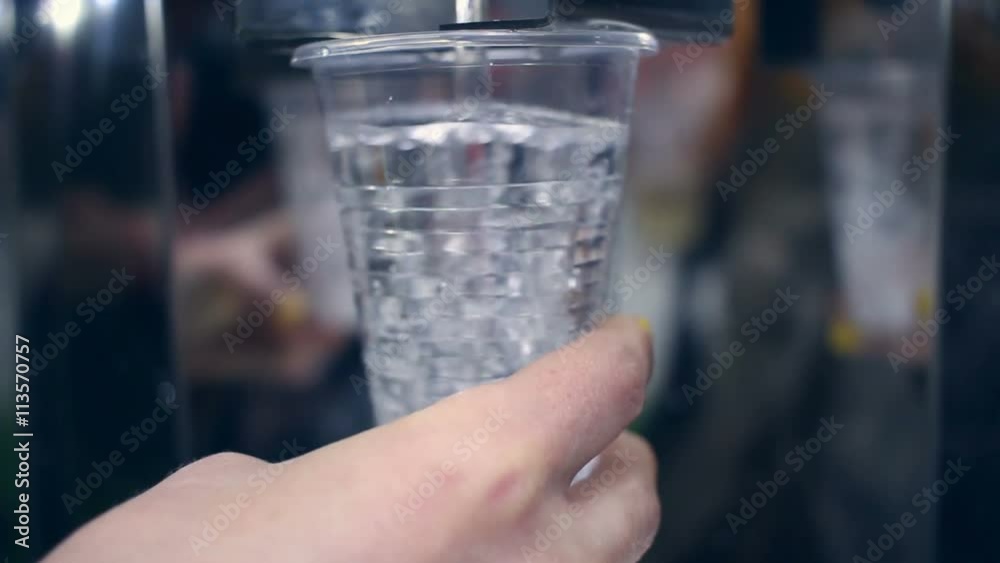 Water flowing into plastic cup. Water cooler. Closeup of hand holding ...