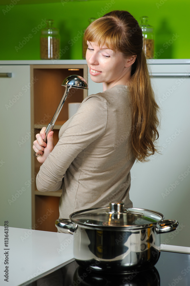 Girl on kitchen with a ladle. Smiling redhead woman with ladle cooking ...