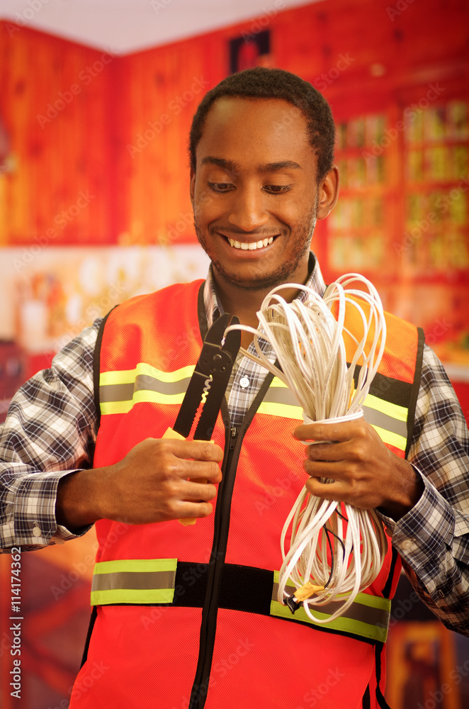 Young electrical worker wearing safety vest, holding cables and cable ...