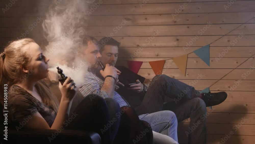 A group of people vaping, inhaling and exhaling large clouds of smoke ...