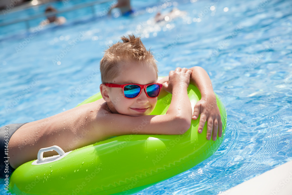 Little boy swimming in the pool with big bright green rubber ring ...