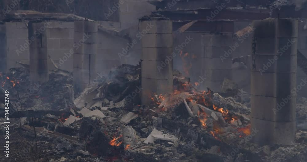 Pile of flaming rubble surrounding a concrete foundation support of a ...
