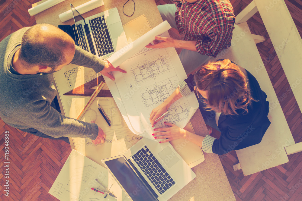 Young group of people discussing business plans, with lap-tops, plans ...