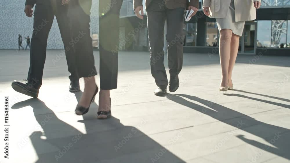 Legs of four business people walking on the pavement in front of office ...